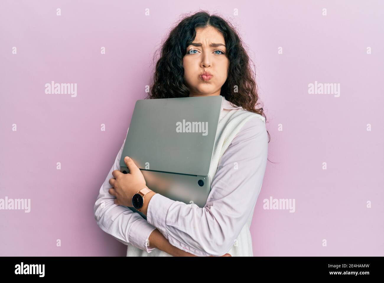 Young brunette woman with curly hair hugging laptop with love puffing ...