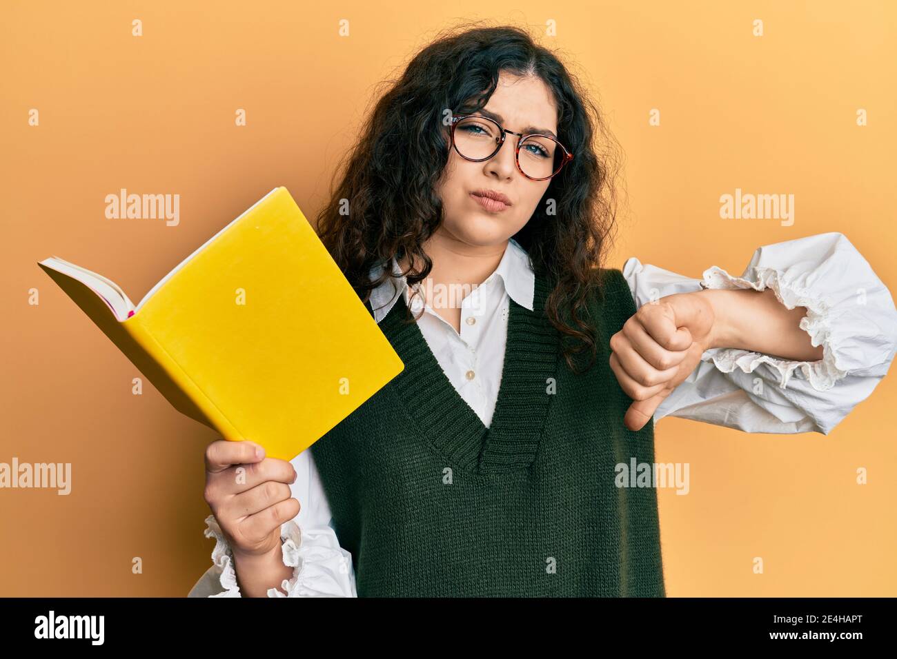 Young brunette woman with curly hair reading a book wearing glasses ...