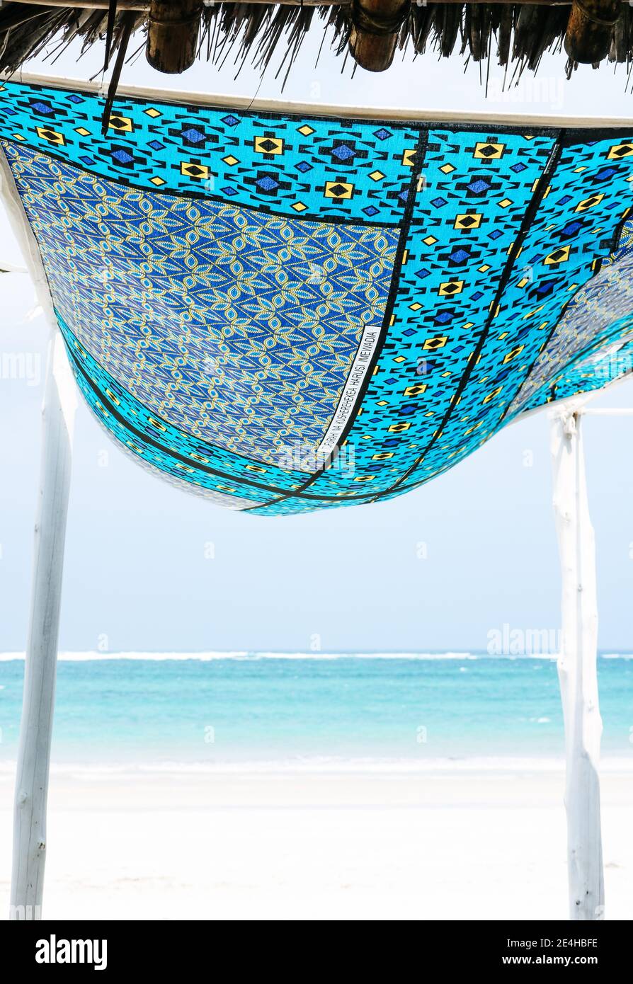 Turquoise patterned cloth blows in the wind in front of a white sanded ...