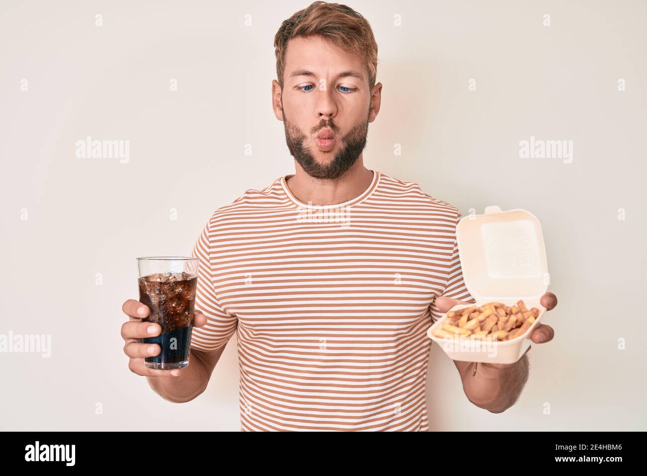 Young caucasian man eating fast food making fish face with mouth and ...