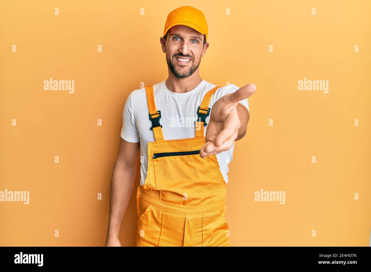 Young handsome man wearing handyman uniform over yellow background ...