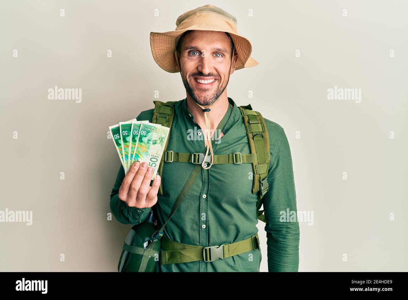 Handsome man with beard wearing explorer hat holding 50 shekels looking ...