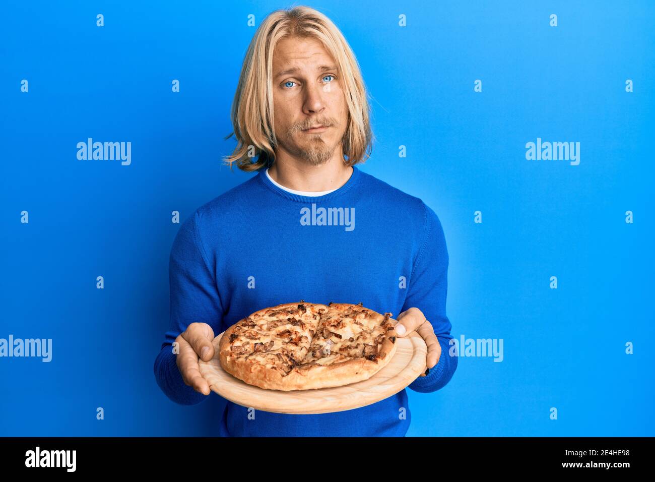 Caucasian young man with long hair holding italian pizza depressed and ...