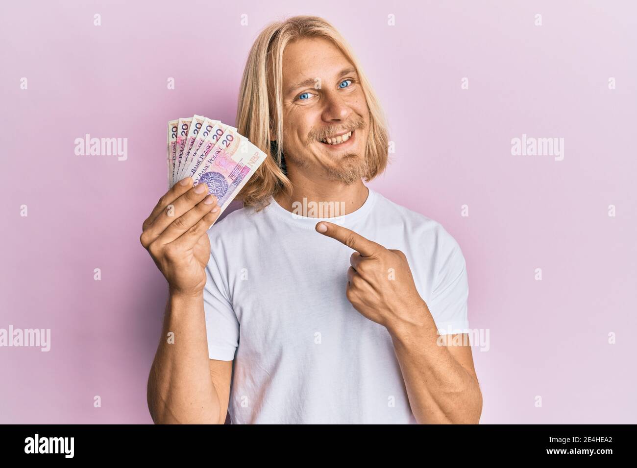 Caucasian young man with long hair holding 20 polish zloty banknotes ...