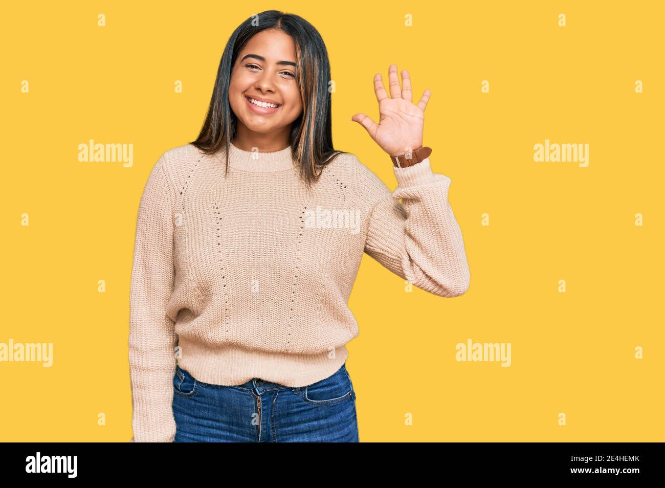 Young latin girl wearing wool winter sweater waiving saying hello happy ...