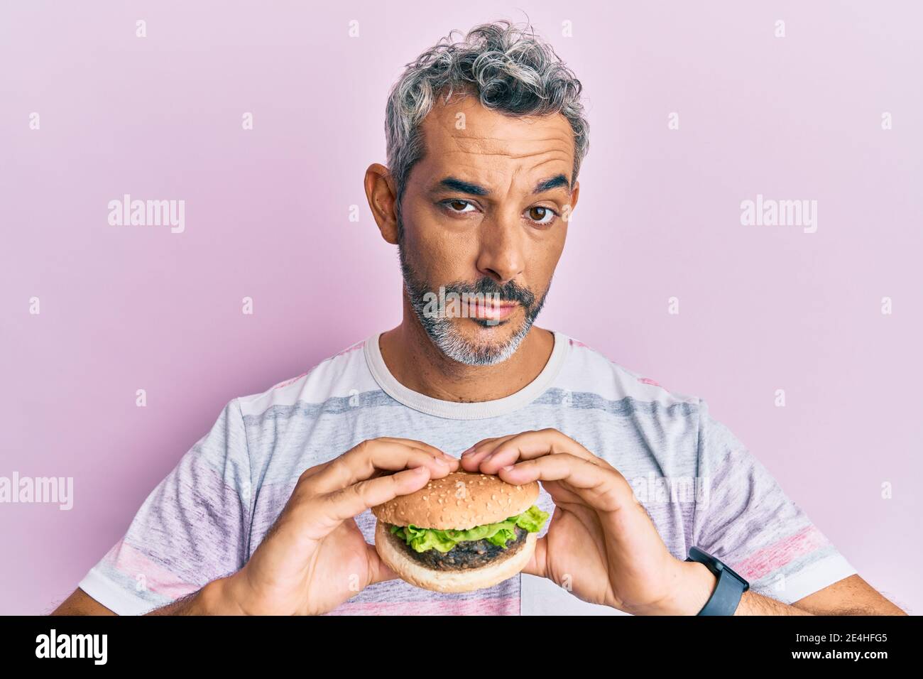 Middle age grey-haired man eating a tasty classic burger skeptic and ...