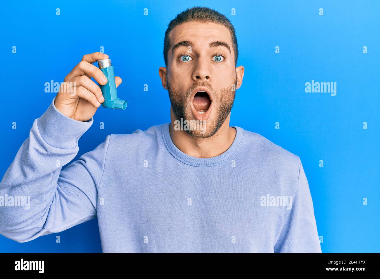 Young caucasian man holding medical asthma inhaler scared and amazed ...