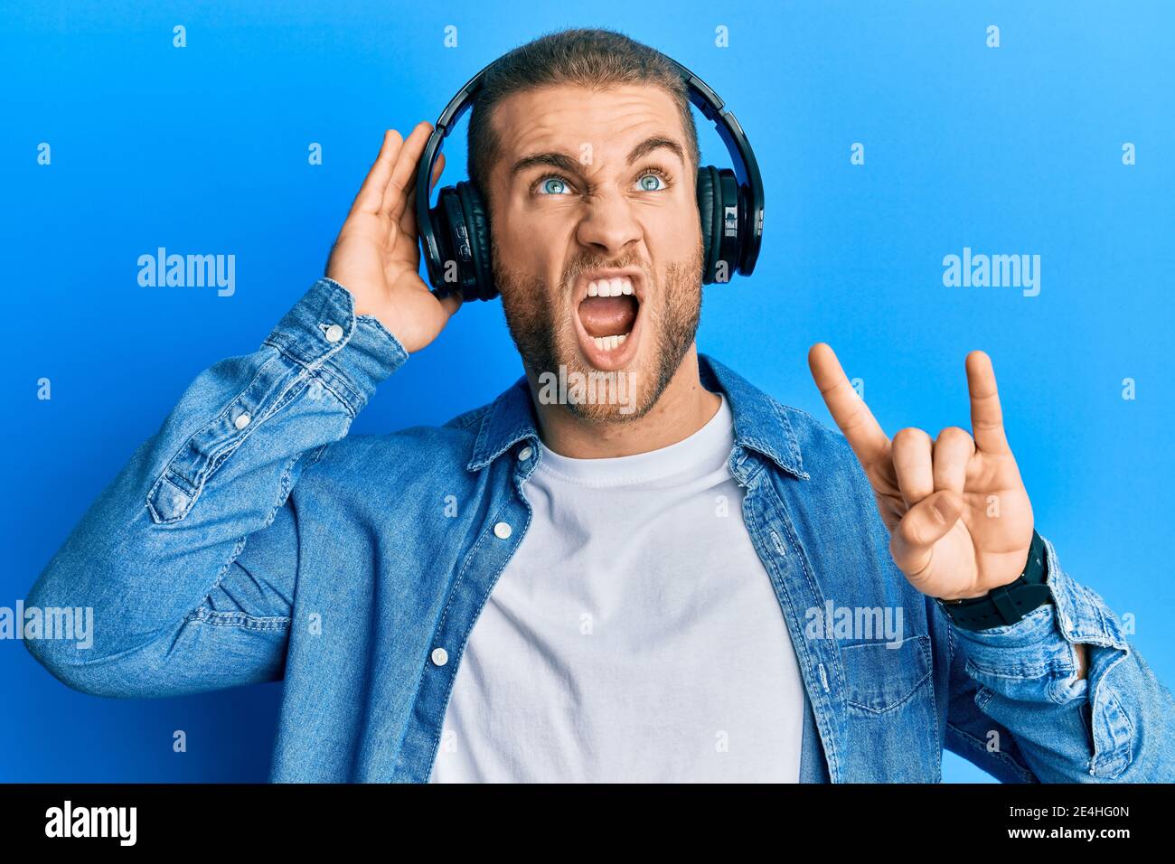 Young caucasian man using headphones and doing rock symbol angry and ...