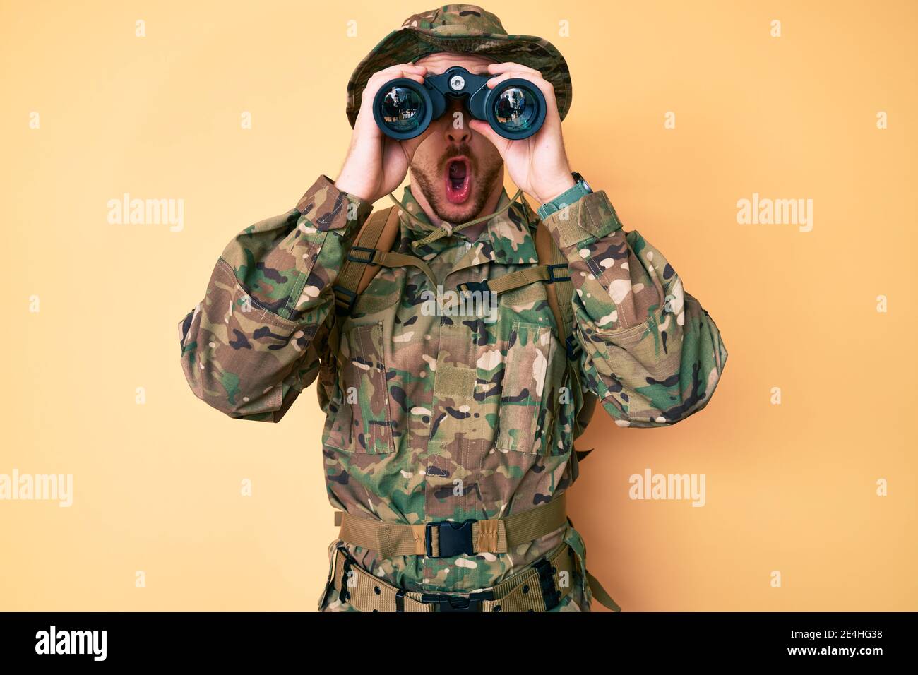Young caucasian man wearing camouflage army uniform using binoculars ...
