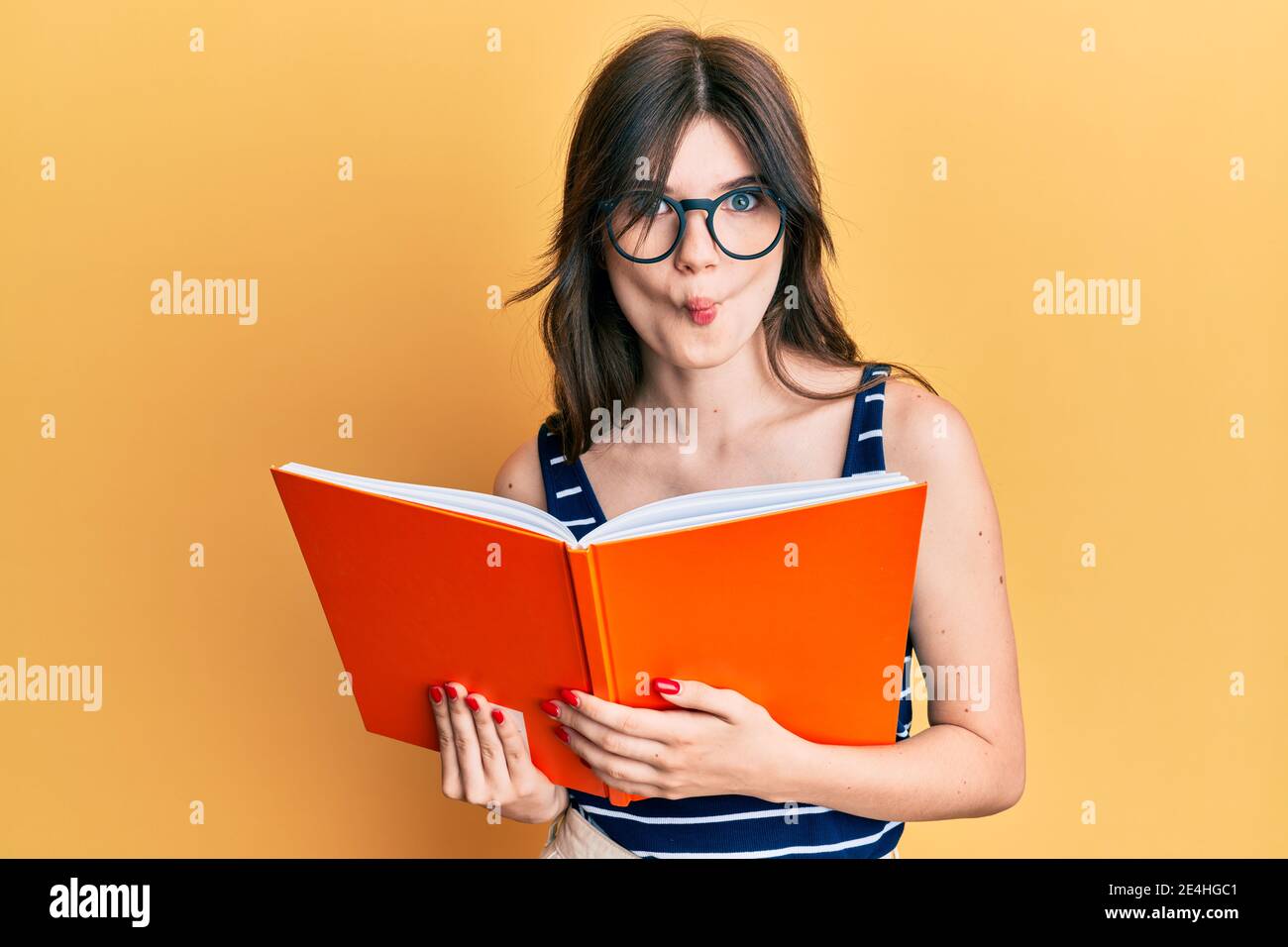 Young beautiful caucasian girl reading a book wearing glasses making ...