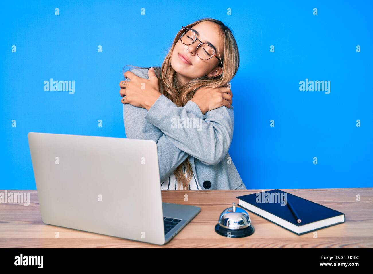 Young beautiful blonde woman sitting at hotel reception hugging oneself ...