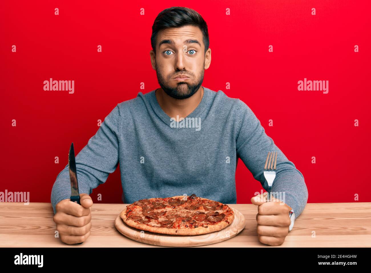 Handsome hispanic man eating tasty pepperoni pizza puffing cheeks with ...