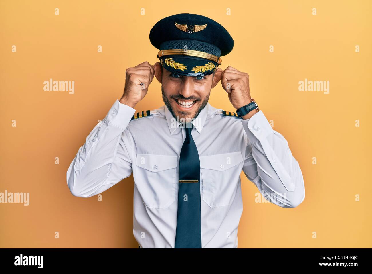 Handsome hispanic man wearing airplane pilot uniform smiling pulling ...