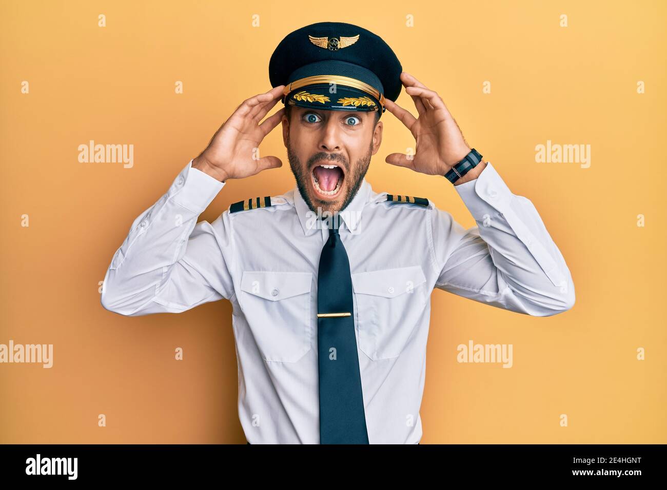 Handsome hispanic man wearing airplane pilot uniform crazy and scared ...