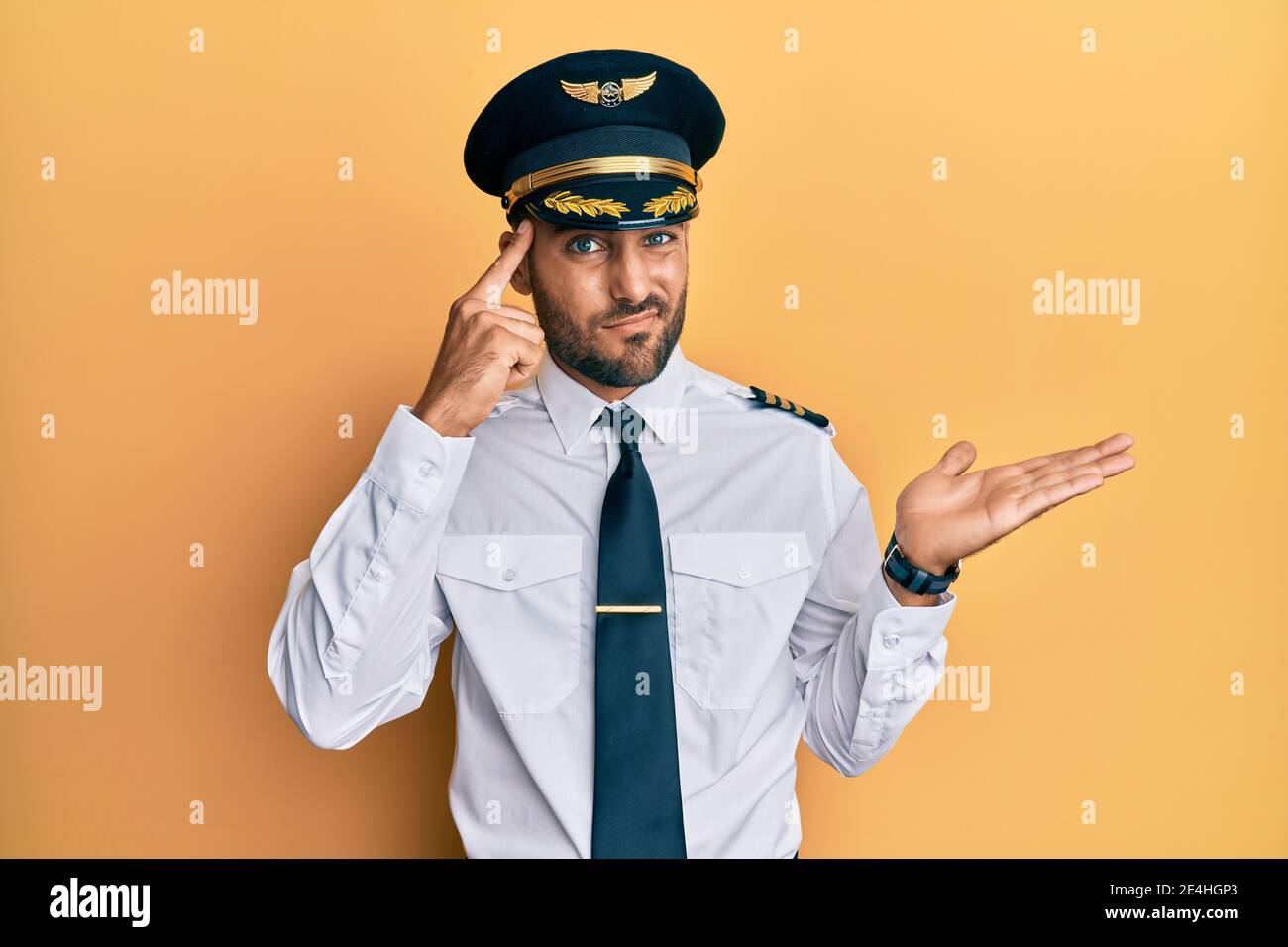 Handsome hispanic man wearing airplane pilot uniform confused and ...