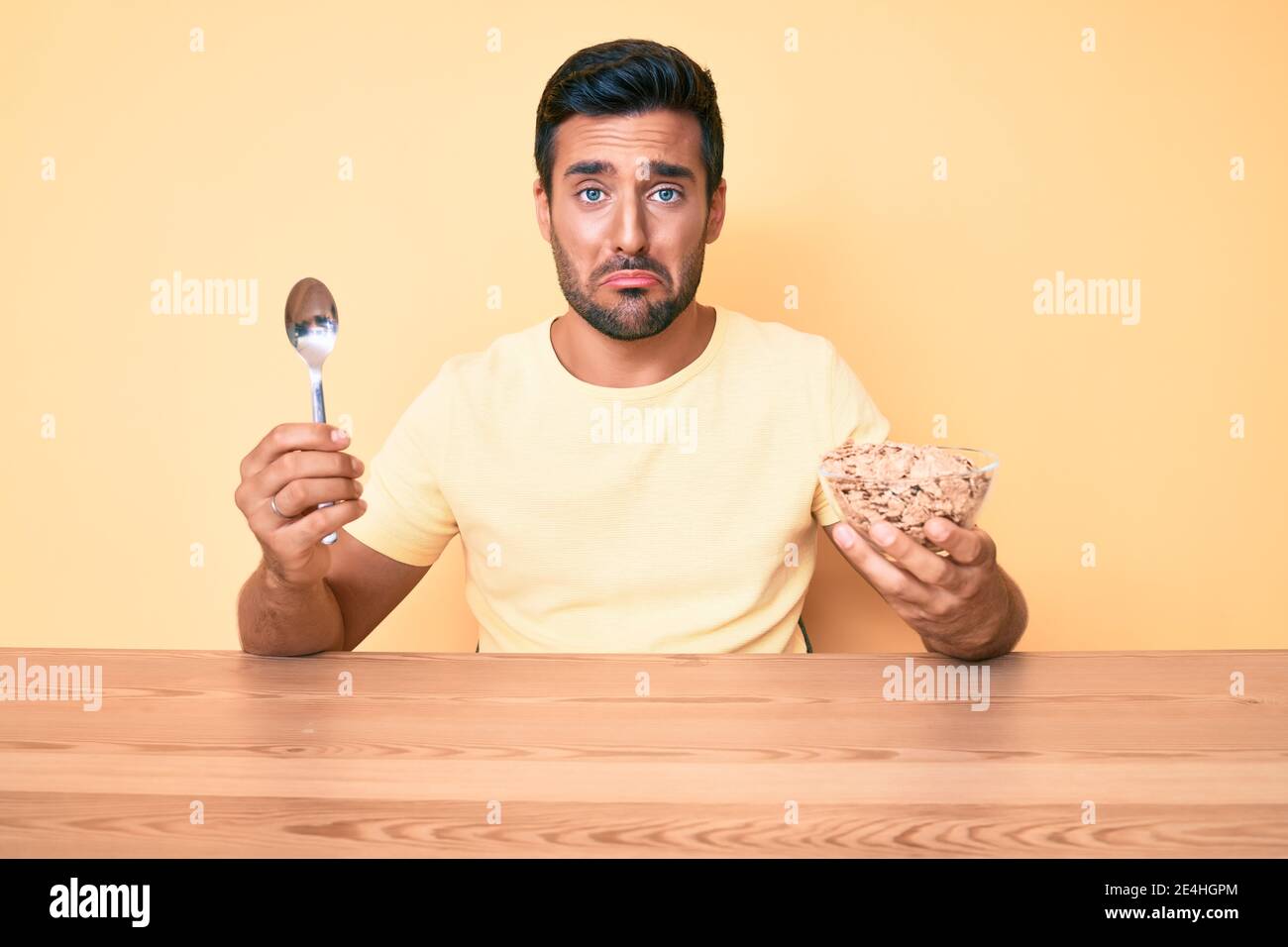 Young handsome hispanic man eating healthy whole grain celears sitting ...
