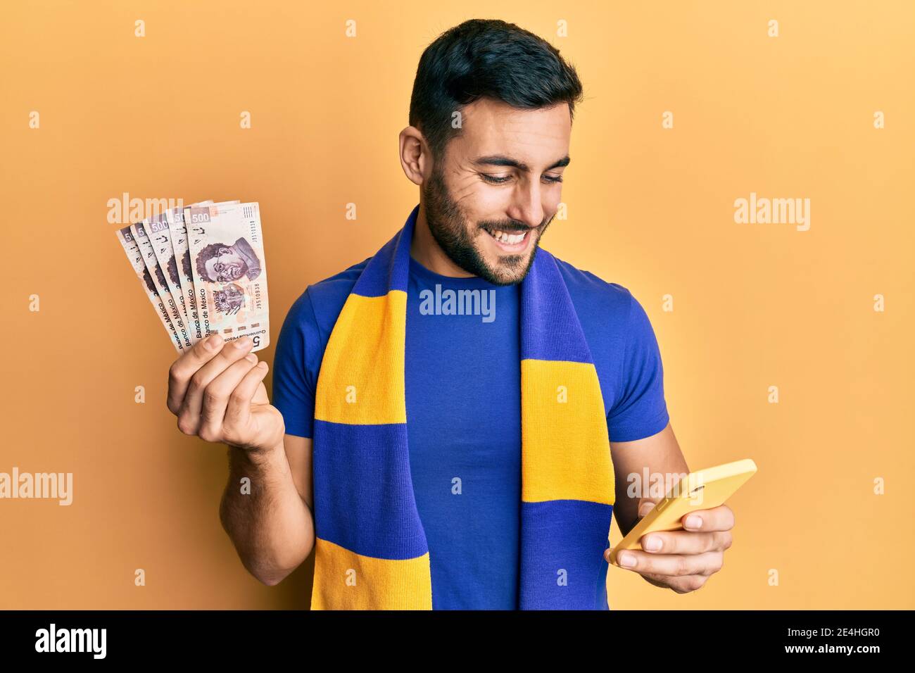 Young hispanic man football supporter using smartphone holding mexican ...