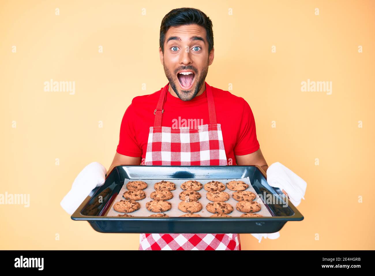 Young hispanic man wearing baker uniform holding homemade cookies ...