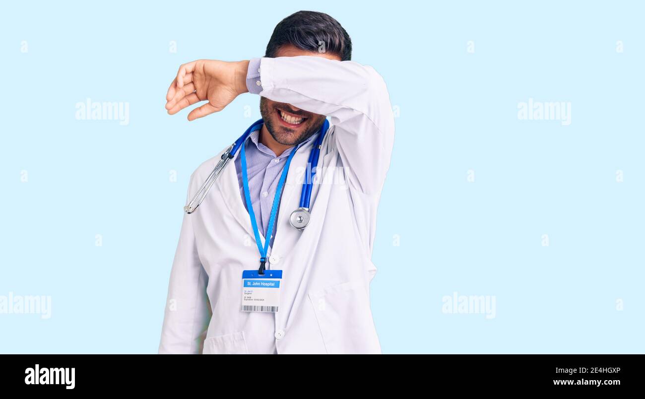 Young hispanic man wearing doctor uniform and stethoscope covering eyes ...