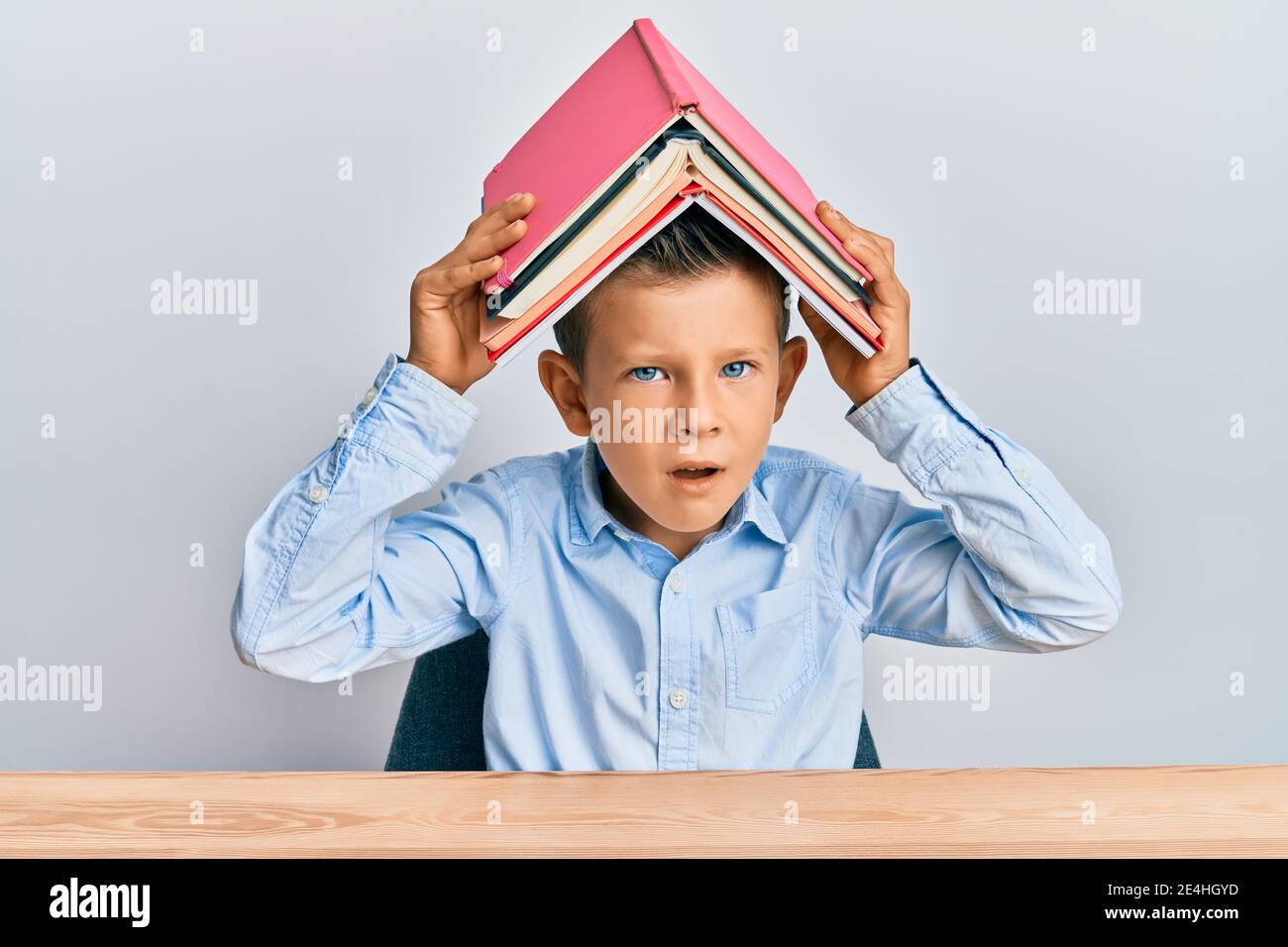 Adorable caucasian kid holding book on head in shock face, looking ...
