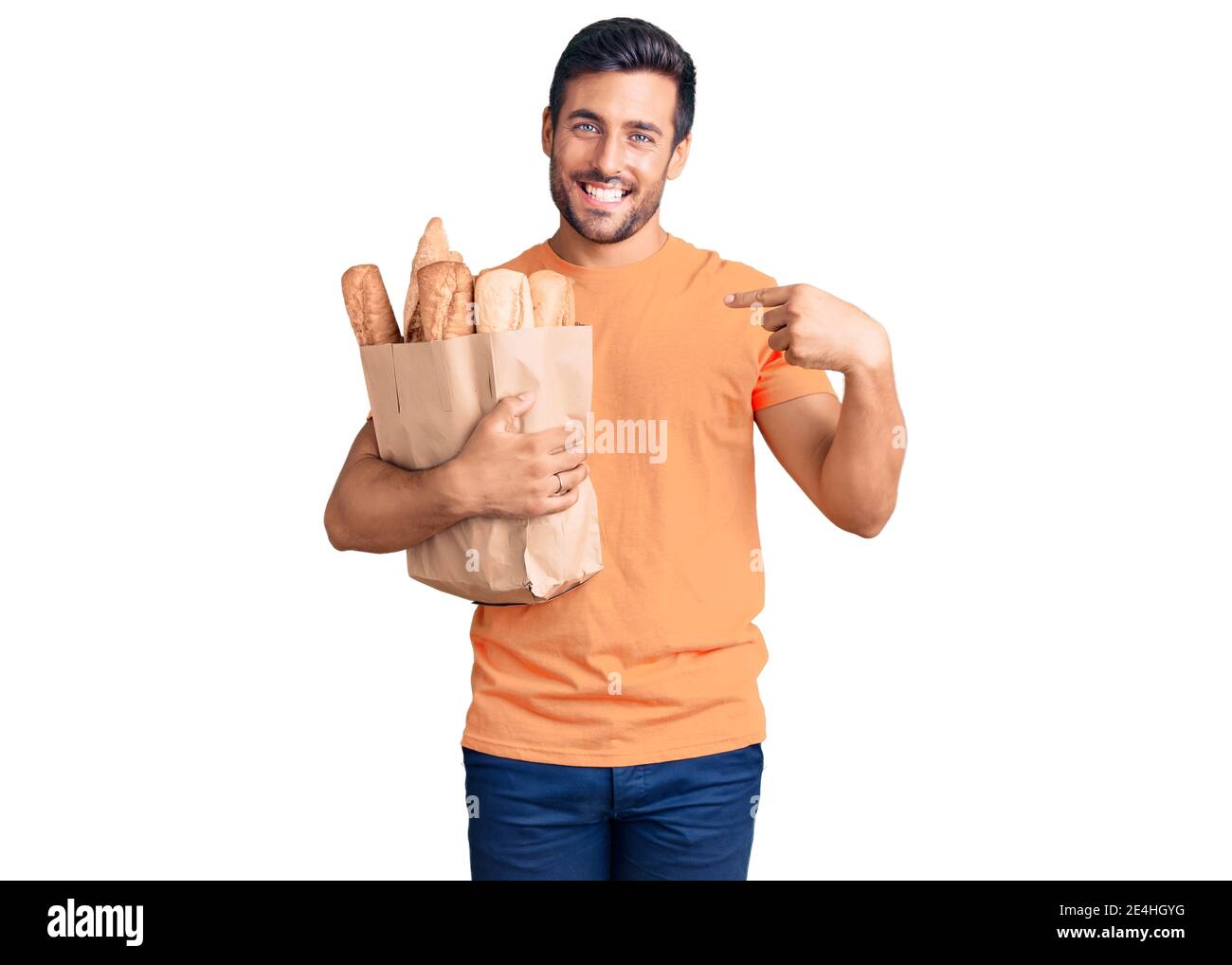 Young hispanic man holding paper bag with bread pointing finger to one ...