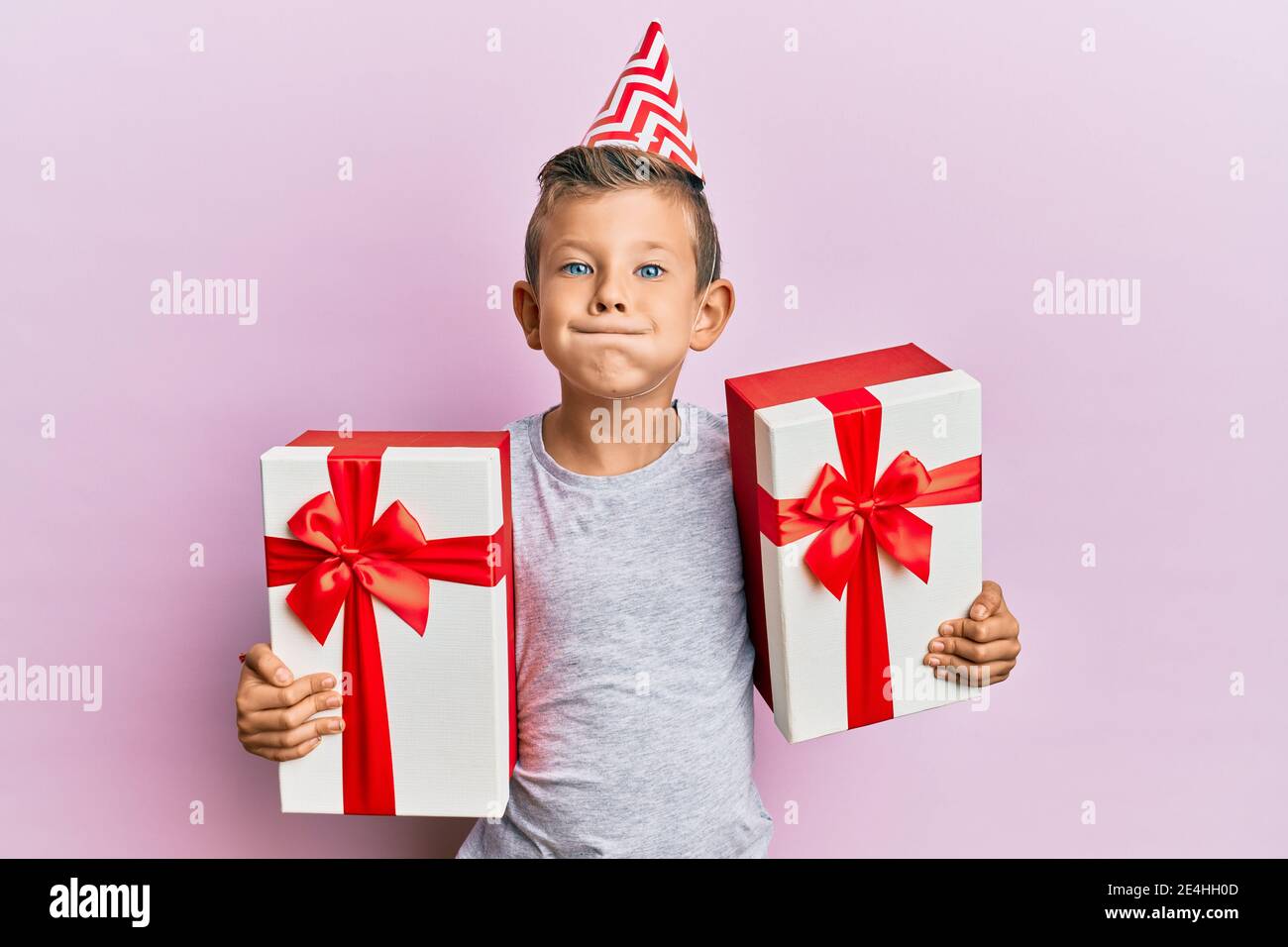Adorable caucasian kid wearing birthday hat holding presents puffing ...
