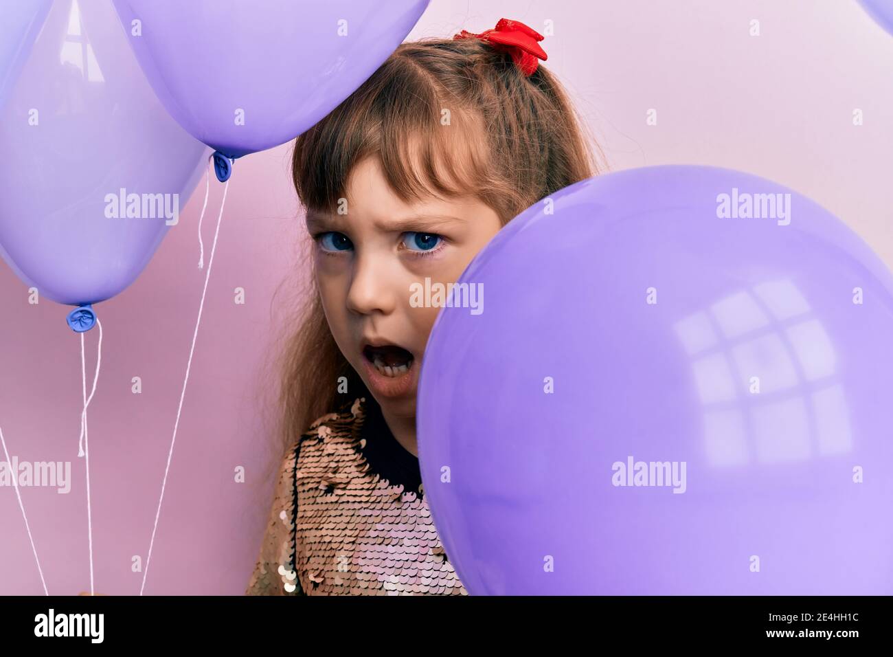 Little caucasian girl kid holding balloons clueless and confused ...