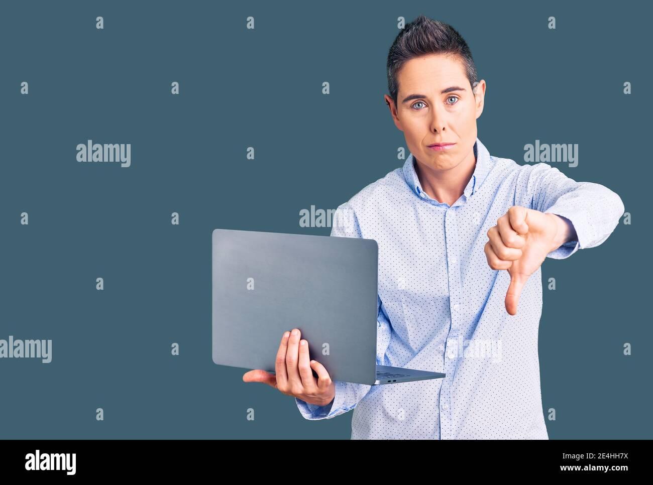 Young woman with short hair holding laptop with angry face, negative ...