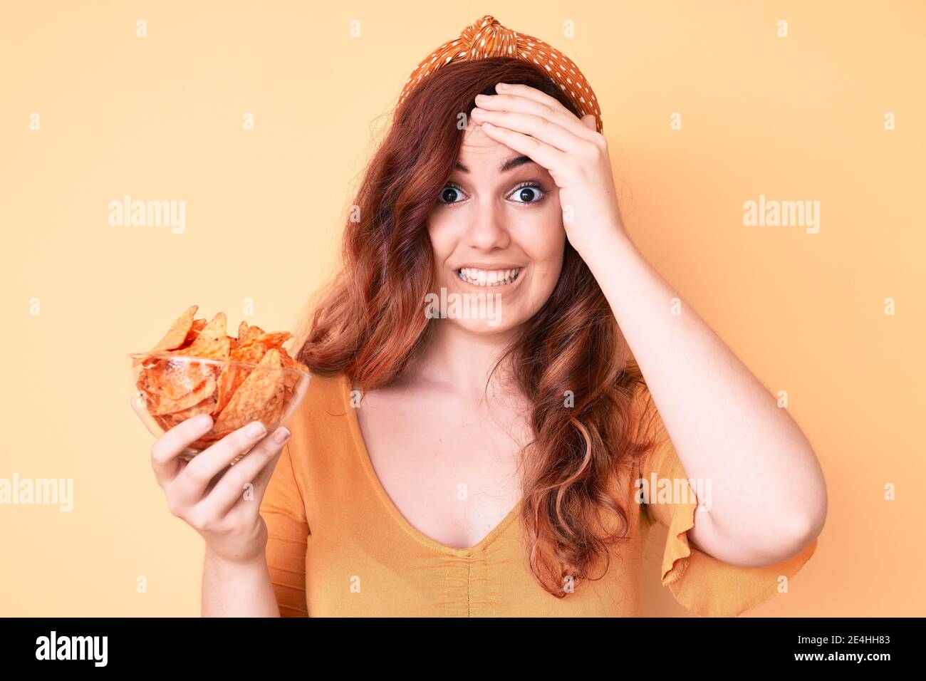 Young beautiful woman holding nachos potato chips stressed and ...