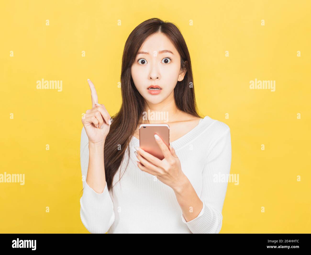 shocked young woman holding mobile phone and pointing to copy space ...