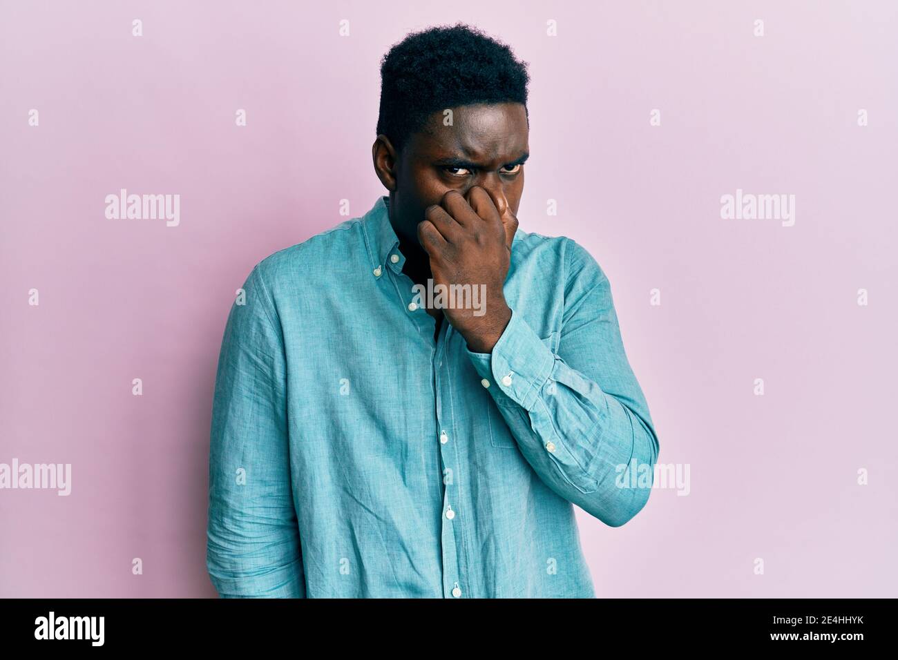 Handsome black man wearing casual clothes smelling something stinky and ...