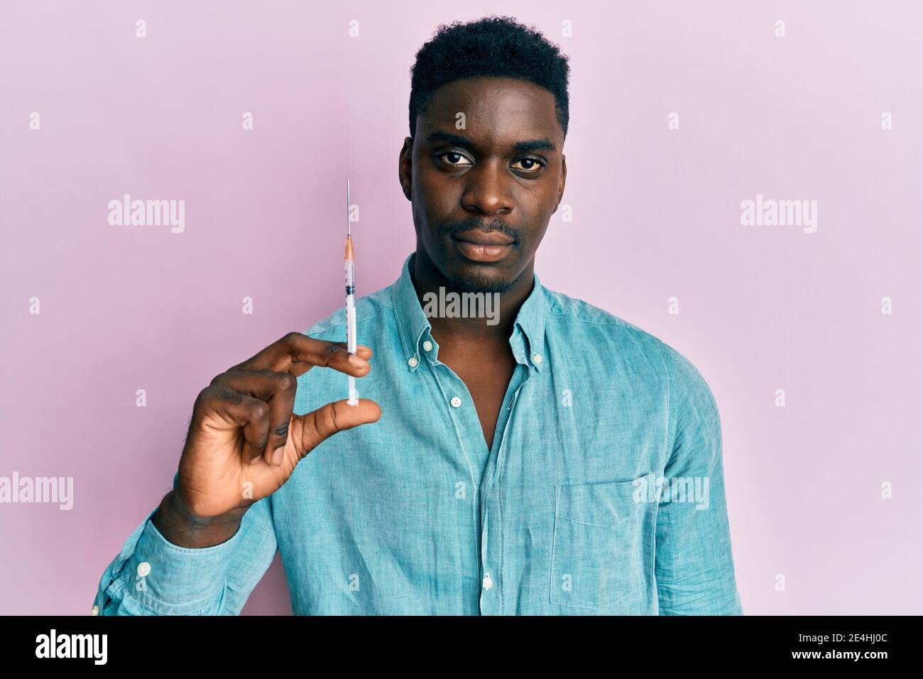 Handsome black man holding syringe thinking attitude and sober ...