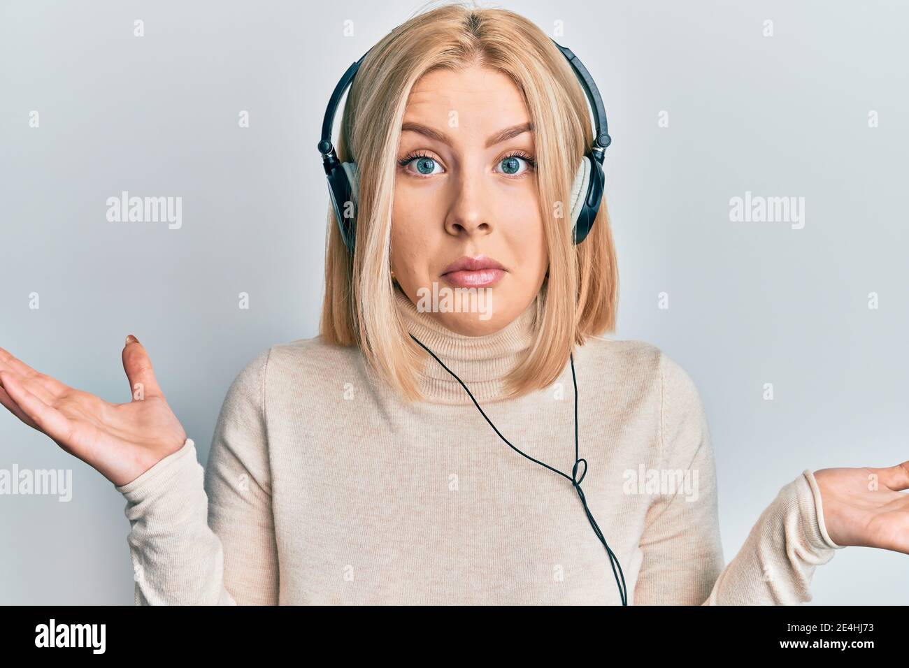 Young blonde woman listening to music using headphones clueless and ...