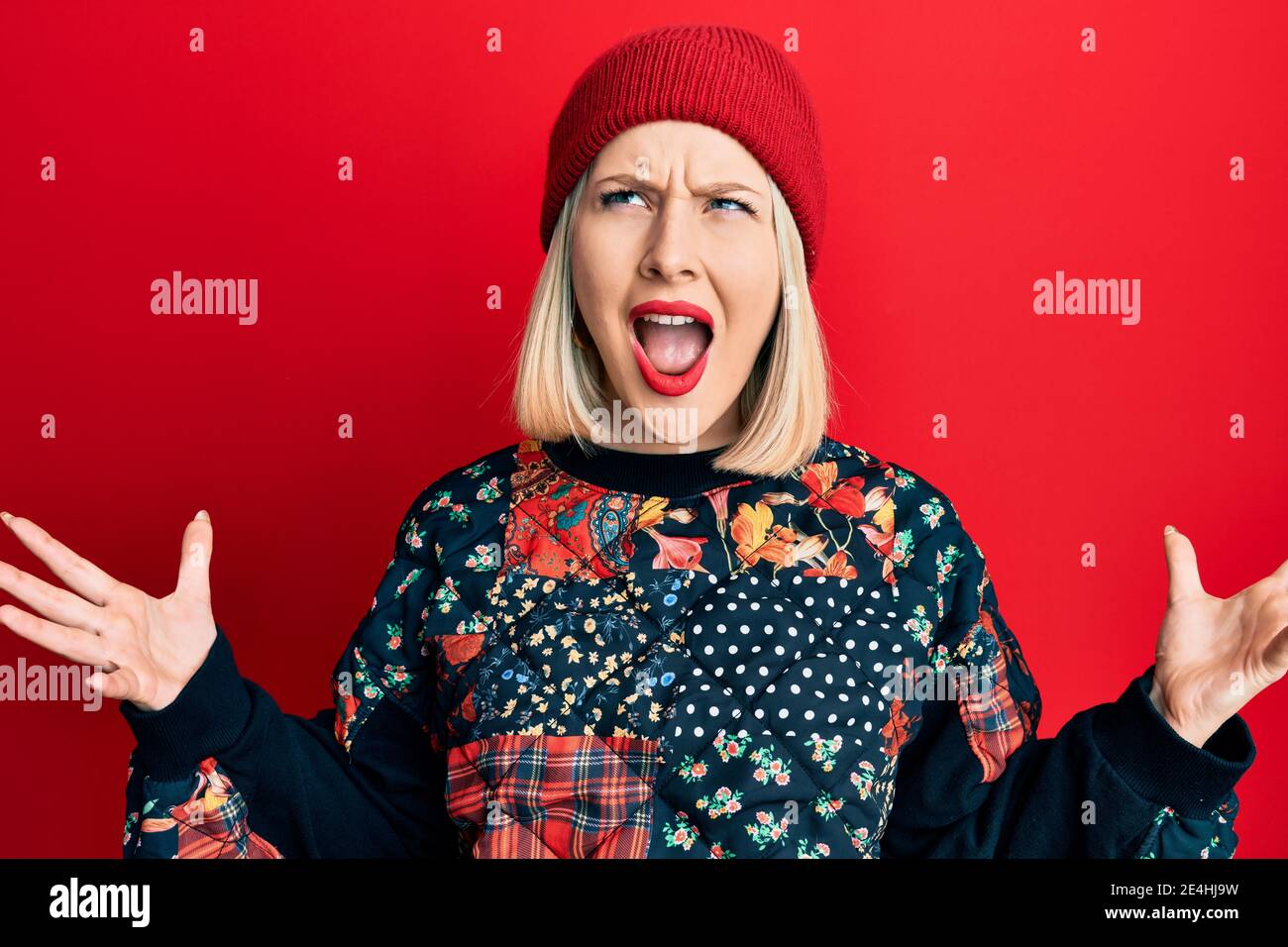 Young blonde woman wearing wool winter cap crazy and mad shouting and ...