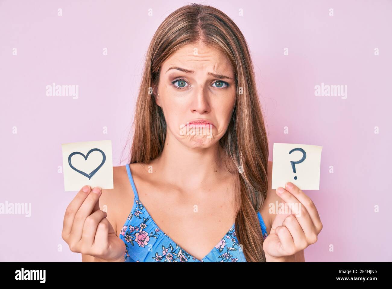 Young blonde girl holding heart and question mark reminder depressed ...
