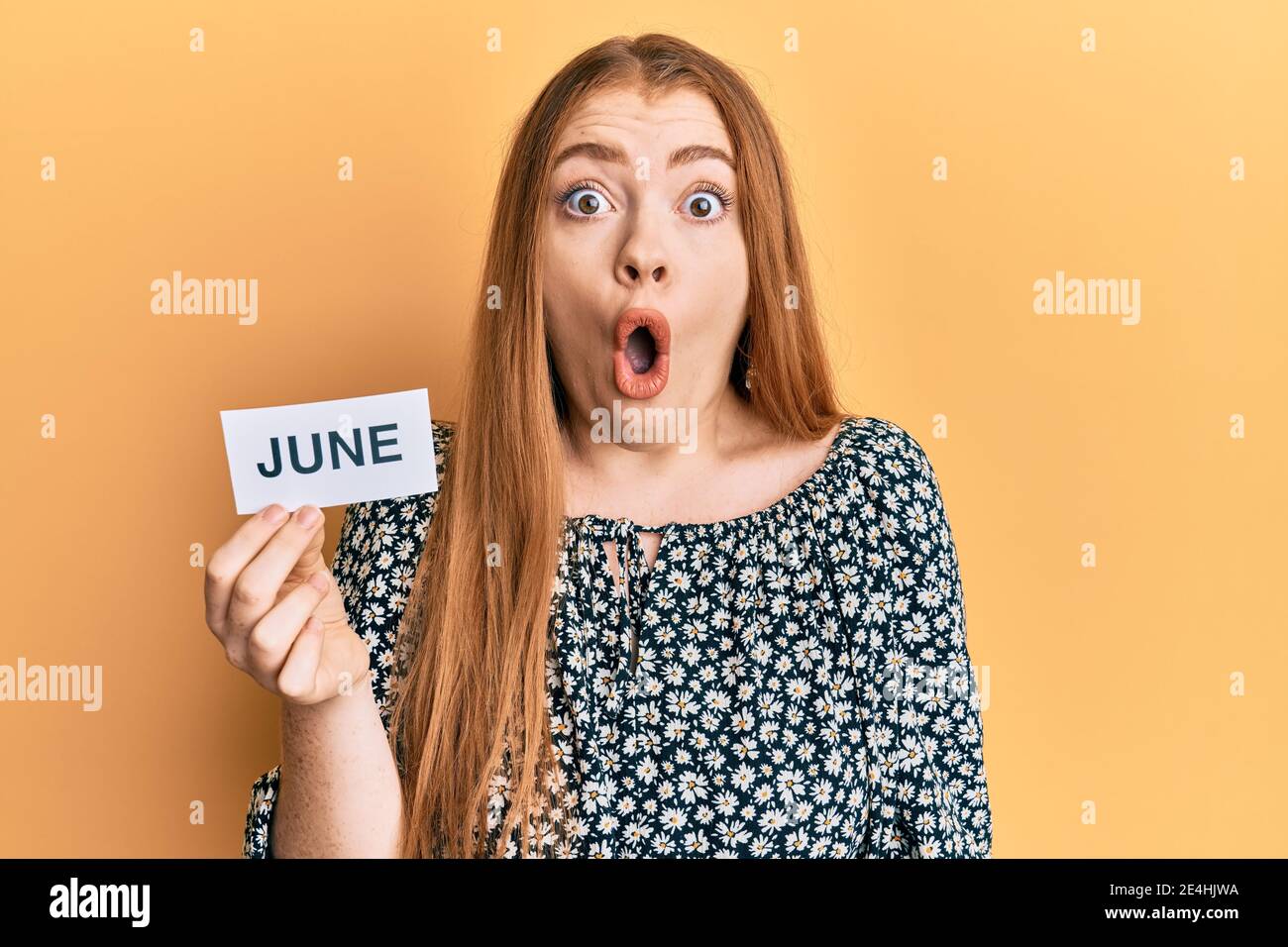 Young beautiful redhead woman holding june word on paper scared and ...