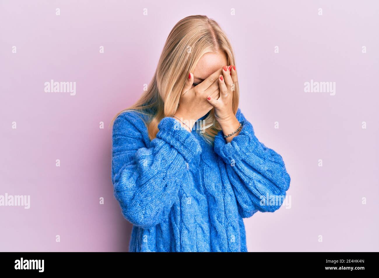 Young blonde girl wearing wool winter sweater with sad expression ...