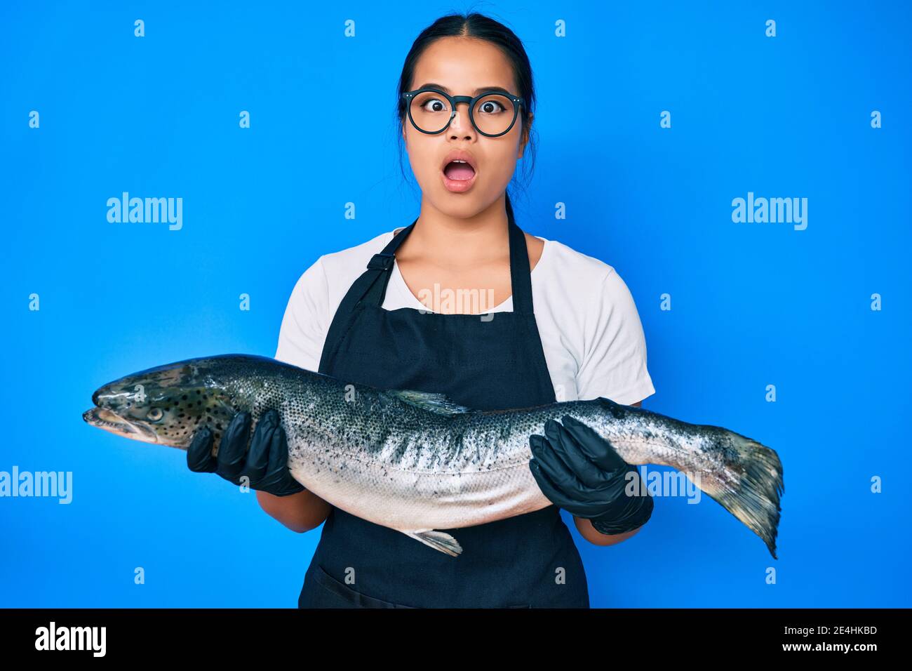 Young beautiful asian girl fishmonger selling fresh raw salmon afraid ...