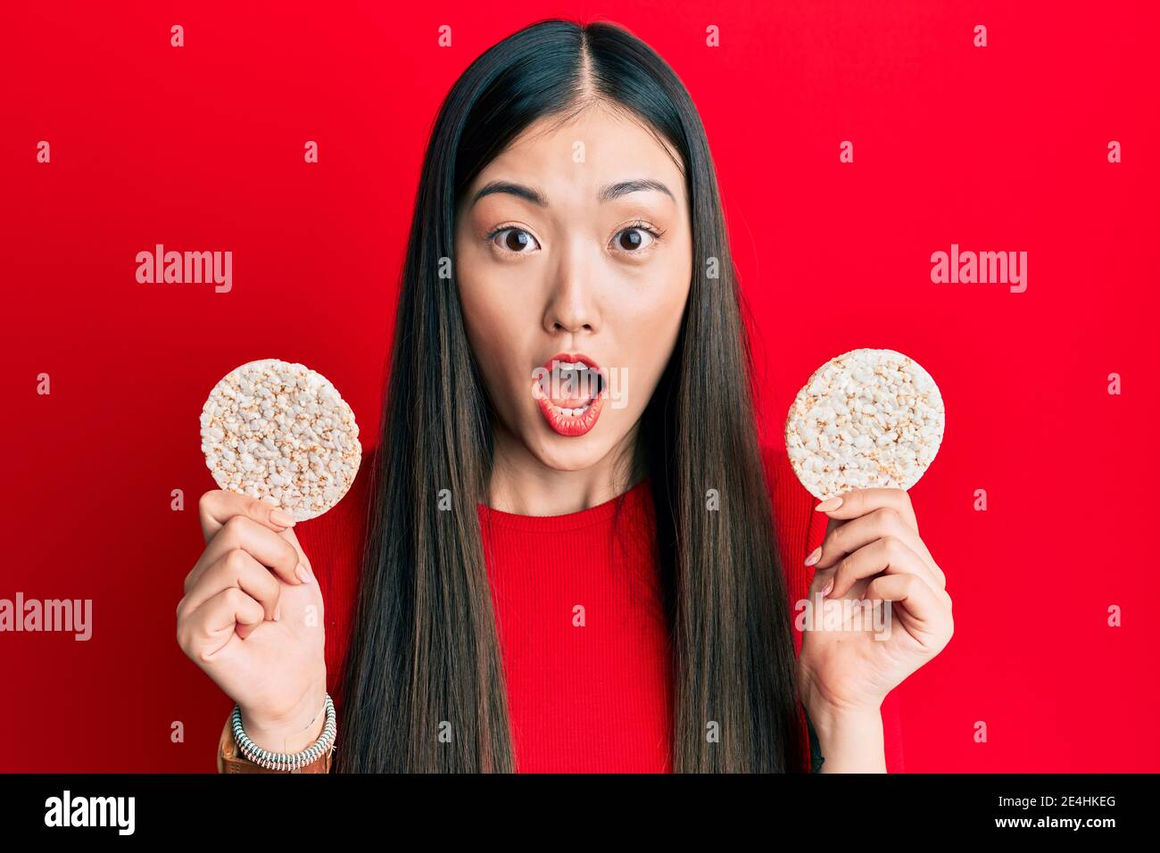 Young chinese woman eating healthy rice crackers afraid and shocked ...
