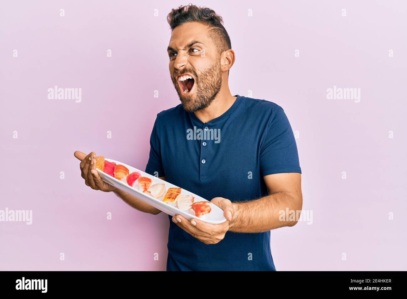 Handsome man with beard showing a plate of sushi angry and mad ...