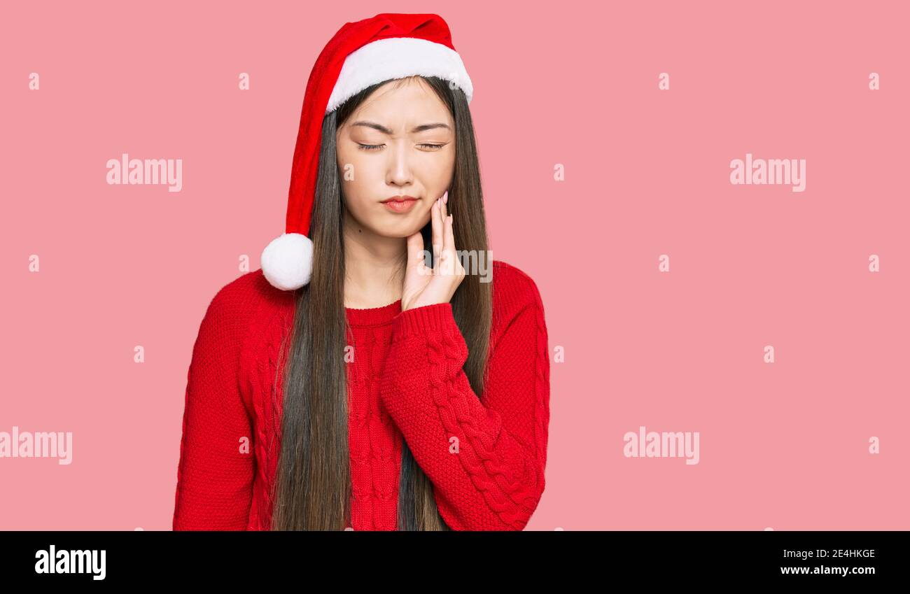 Young chinese woman wearing christmas hat touching mouth with hand with ...