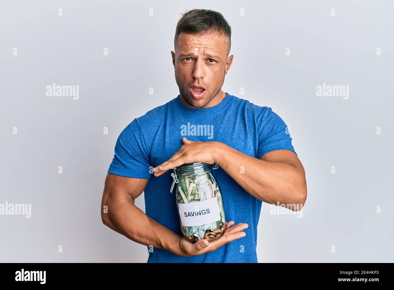 Handsome muscle man holding jar with savings in shock face, looking ...