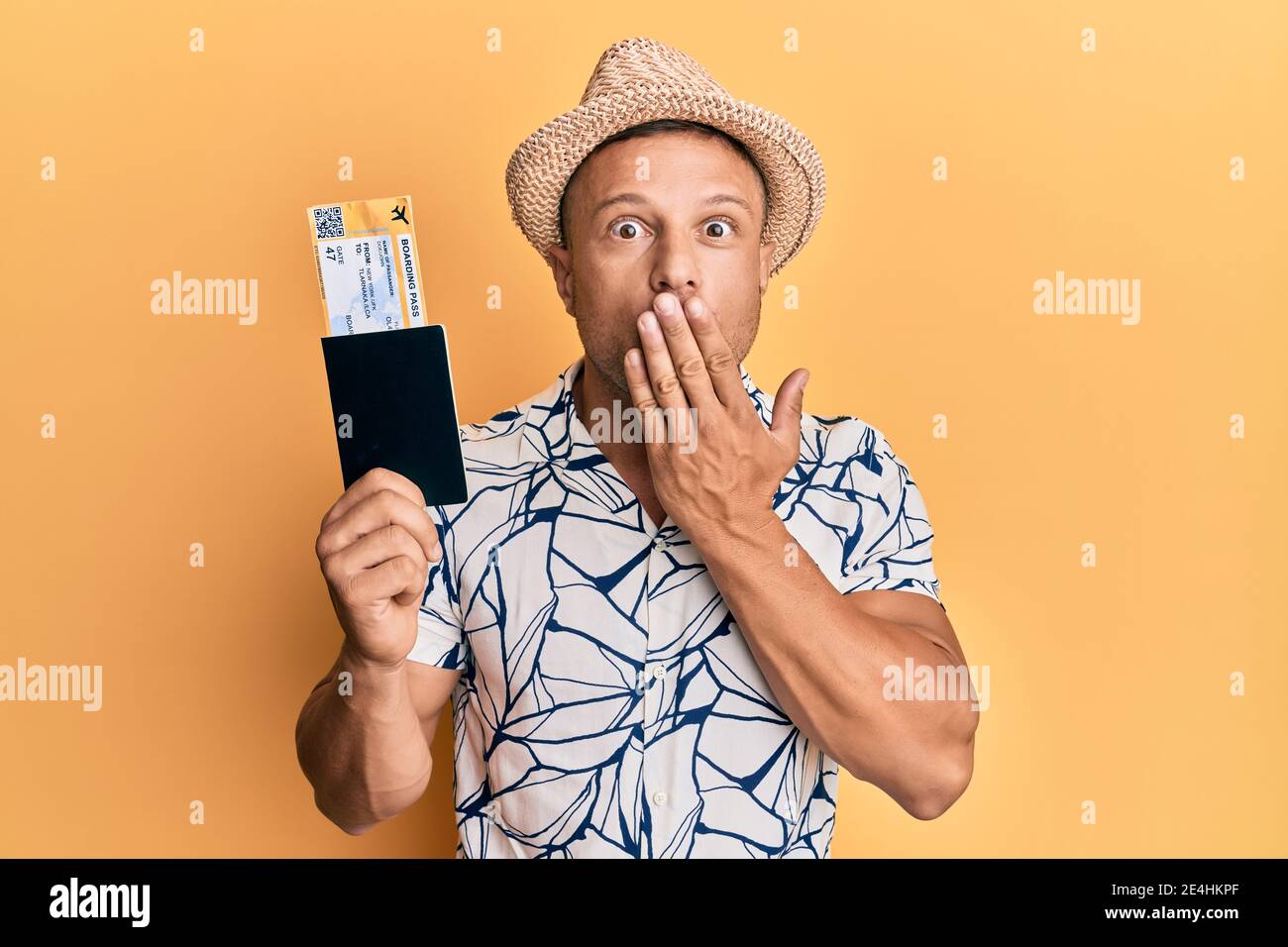 Handsome muscle man holding boarding pass and passport covering mouth ...