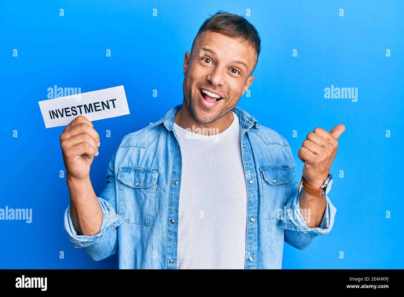 Handsome muscle man holding investment word on paper pointing thumb up ...