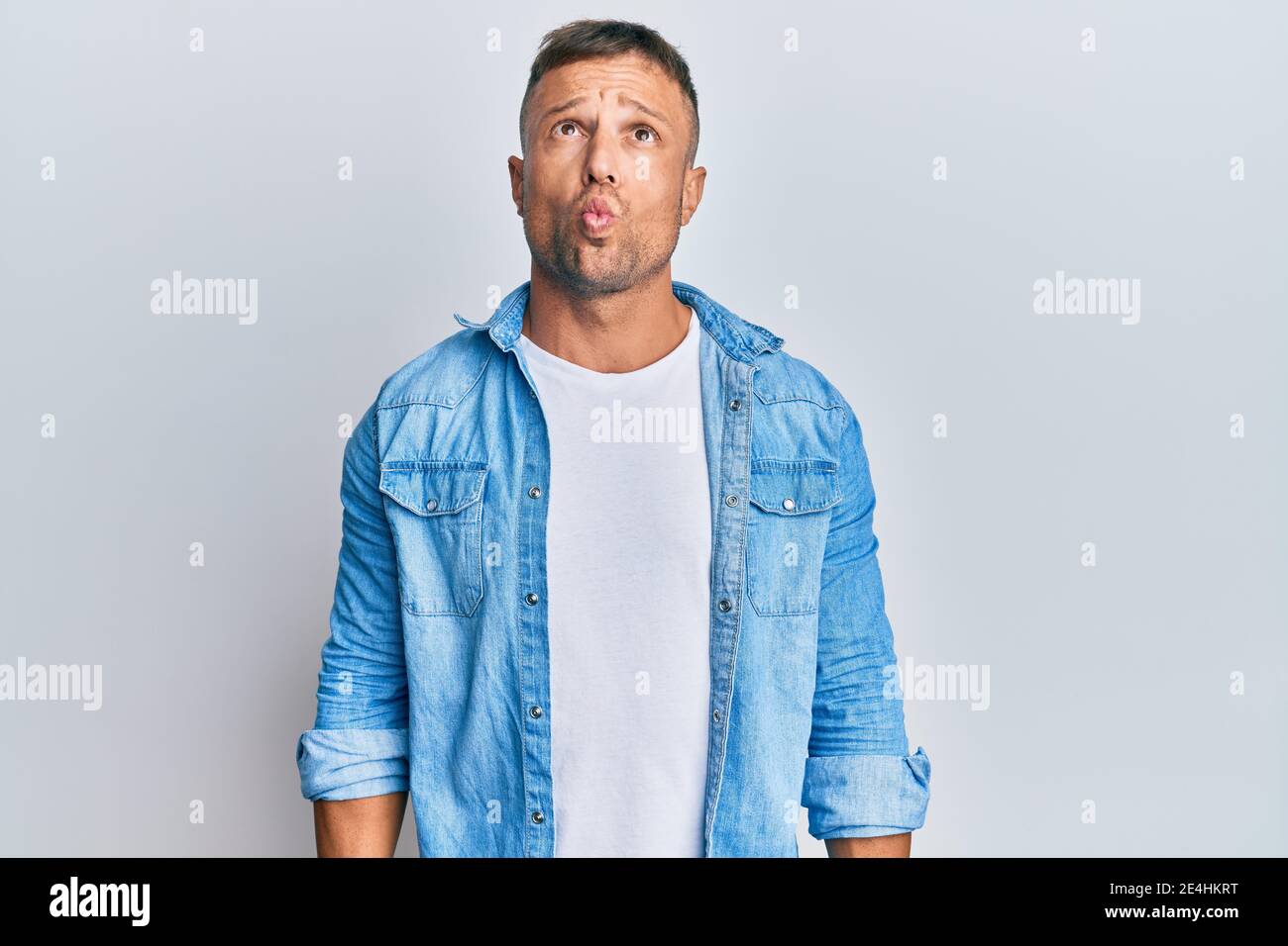 Handsome muscle man wearing casual denim jacket making fish face with ...