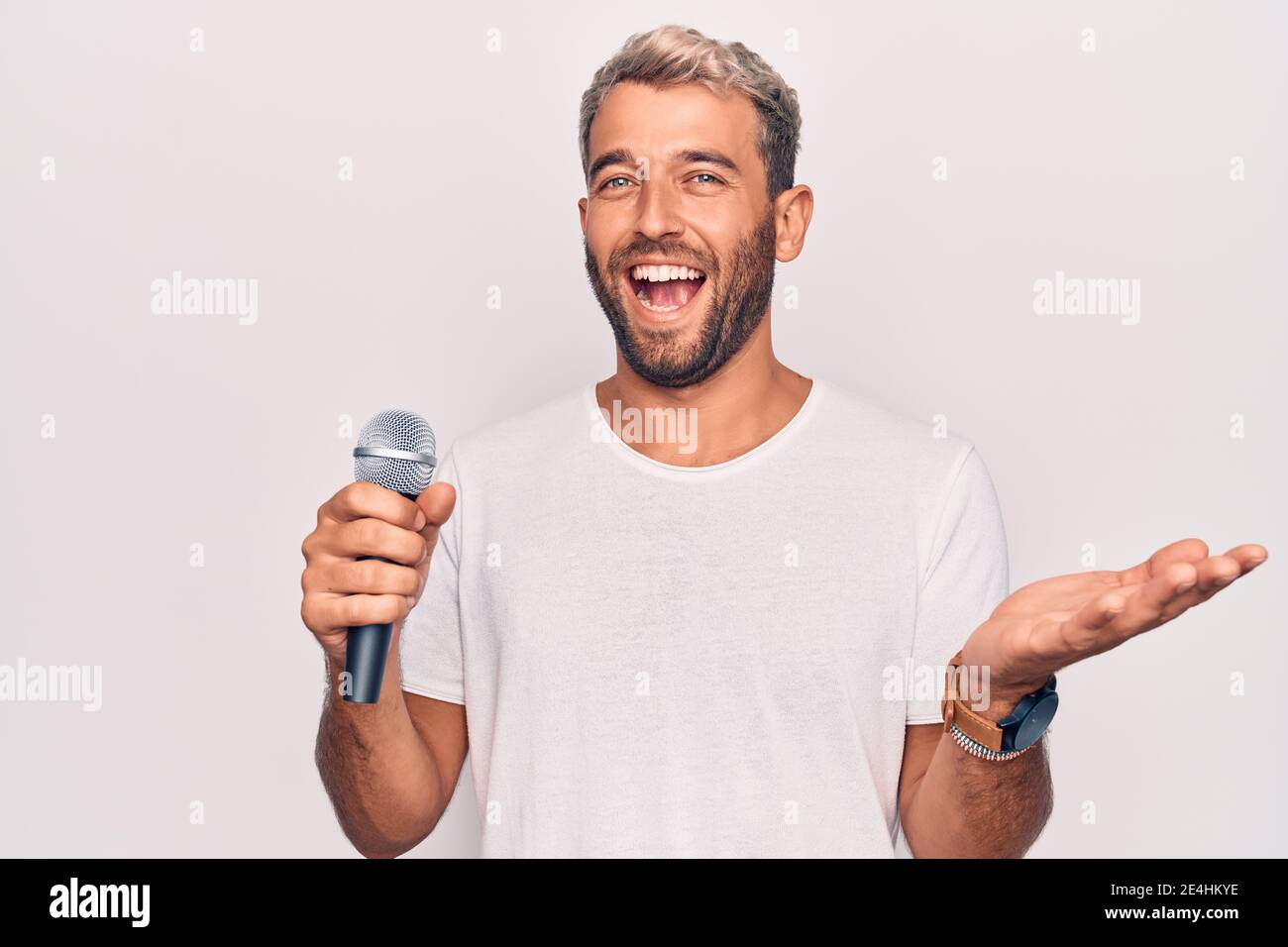 Handsome blond singer man with beard singing song using microphone over white background ...