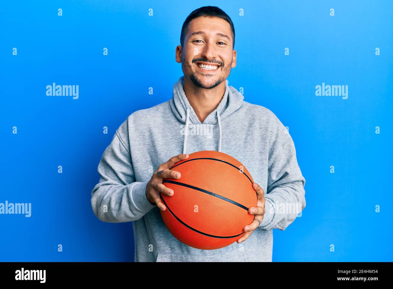 Handsome man with tattoos holding basketball ball smiling with a happy ...