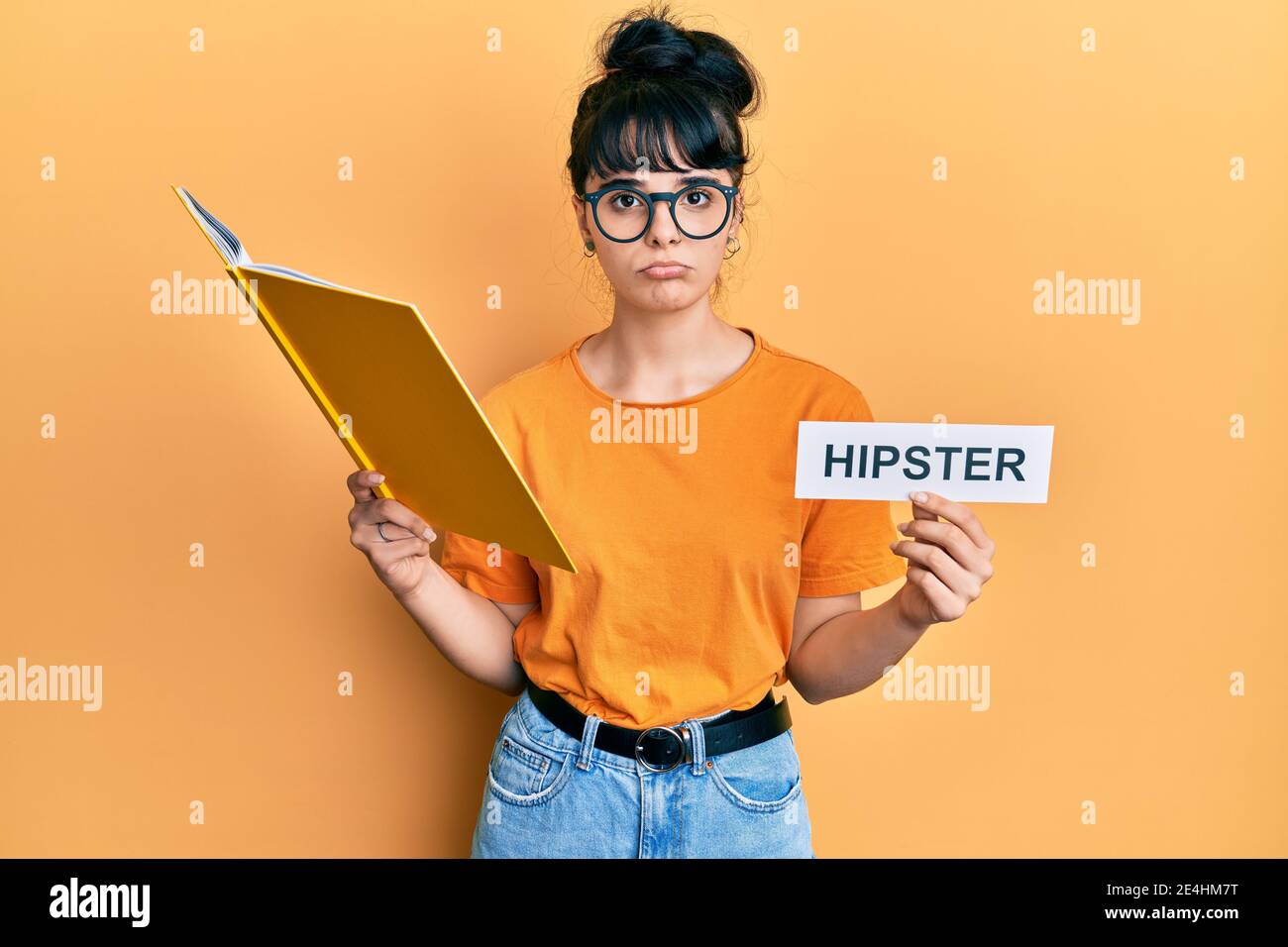 Young hispanic girl reading book and holding paper with hipster message ...