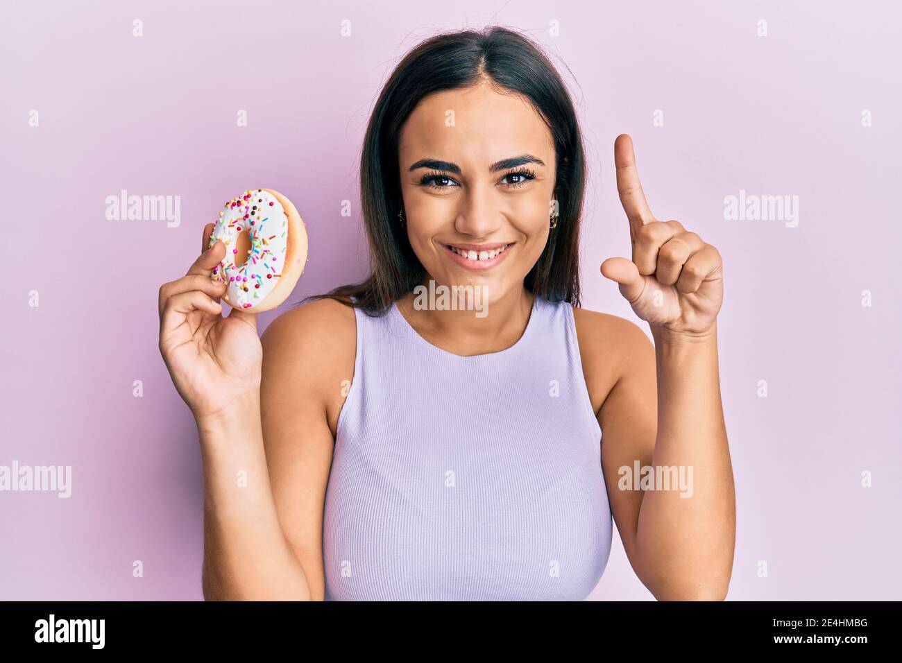 Young brunette woman holding tasty colorful doughnut smiling with an ...
