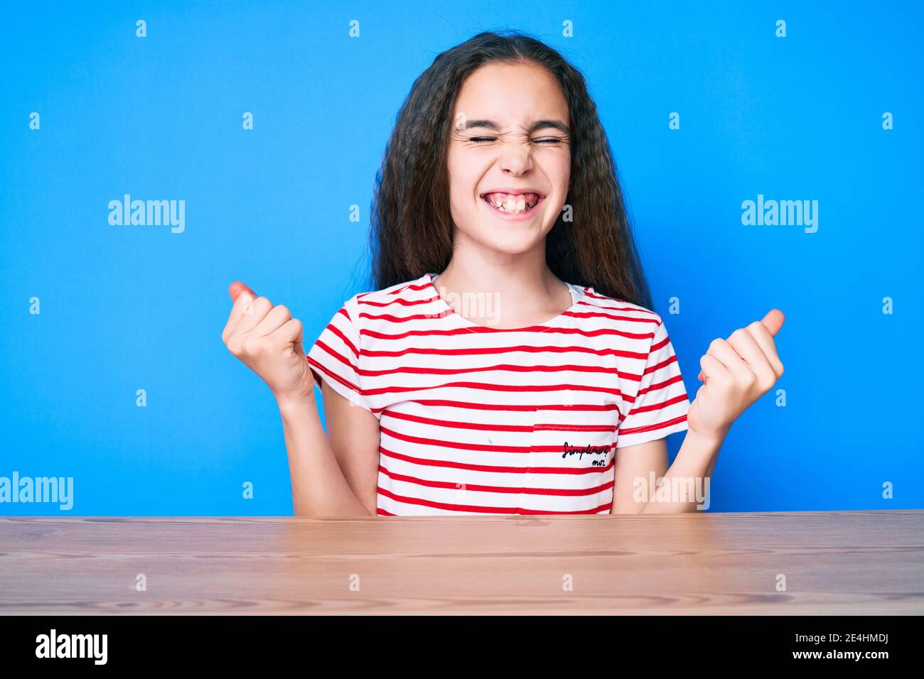Cute hispanic child girl wearing casual clothes sitting on the table ...